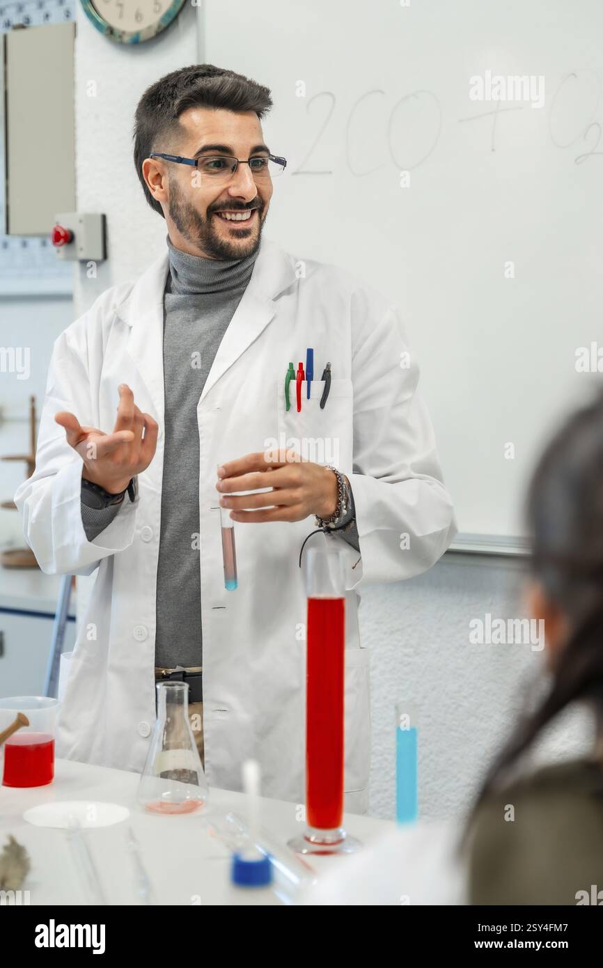 Smiling chemistry teacher showing colorful test tubes and beakers while ...
