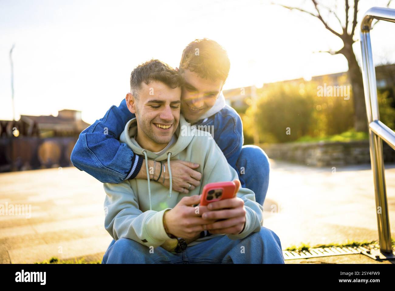 Two men embracing and laughing together while enjoying a smartphone ...