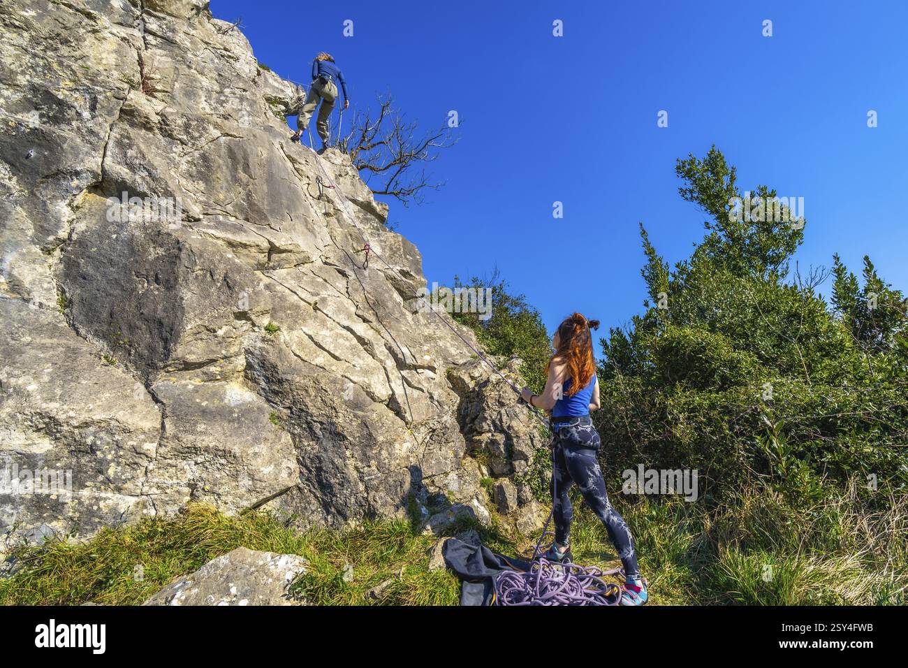 Two female rock climbers scaling steep cliff on bright sunny day ...