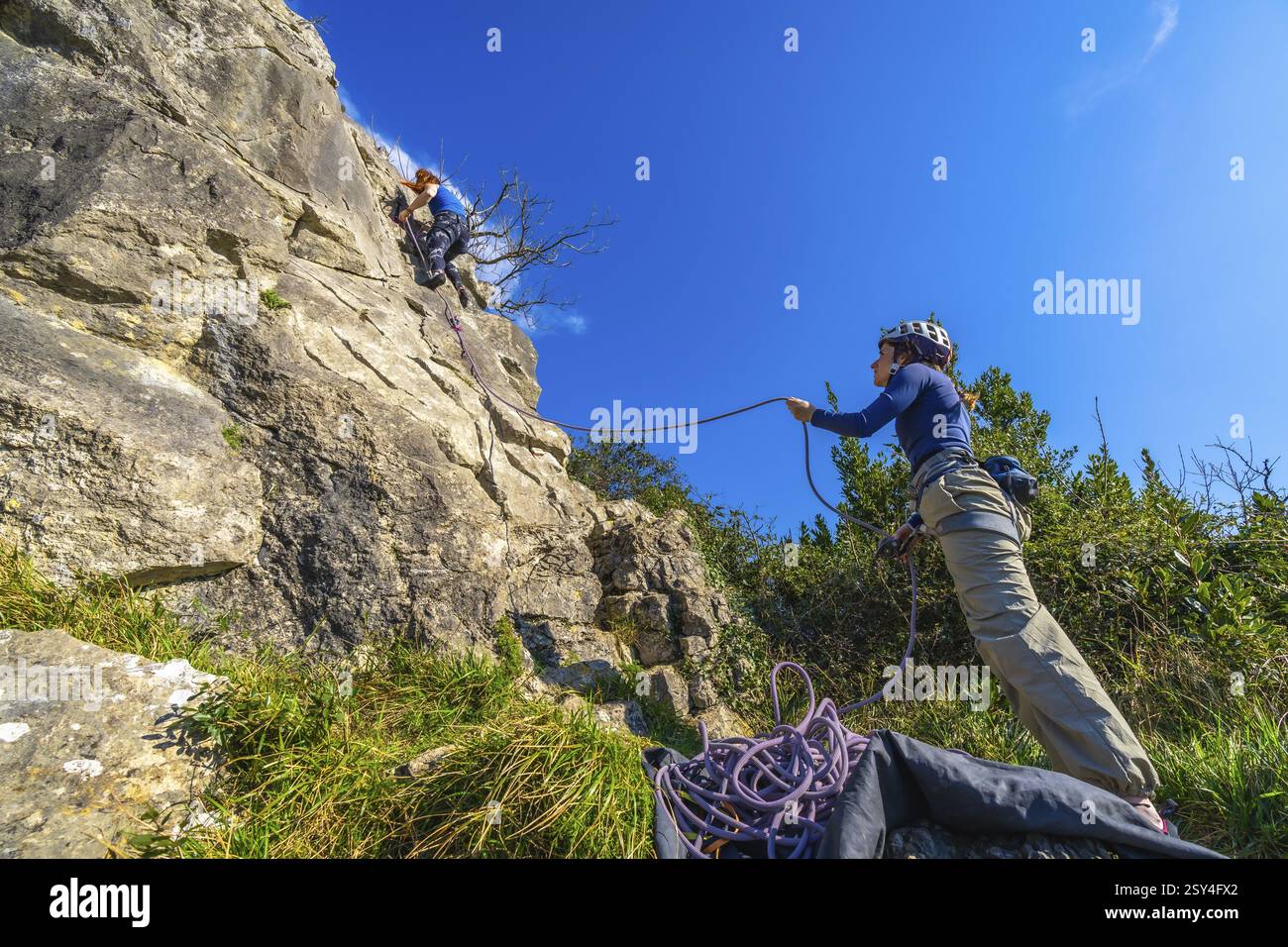 Two female climbers ascending a rock face, one belaying the other ...