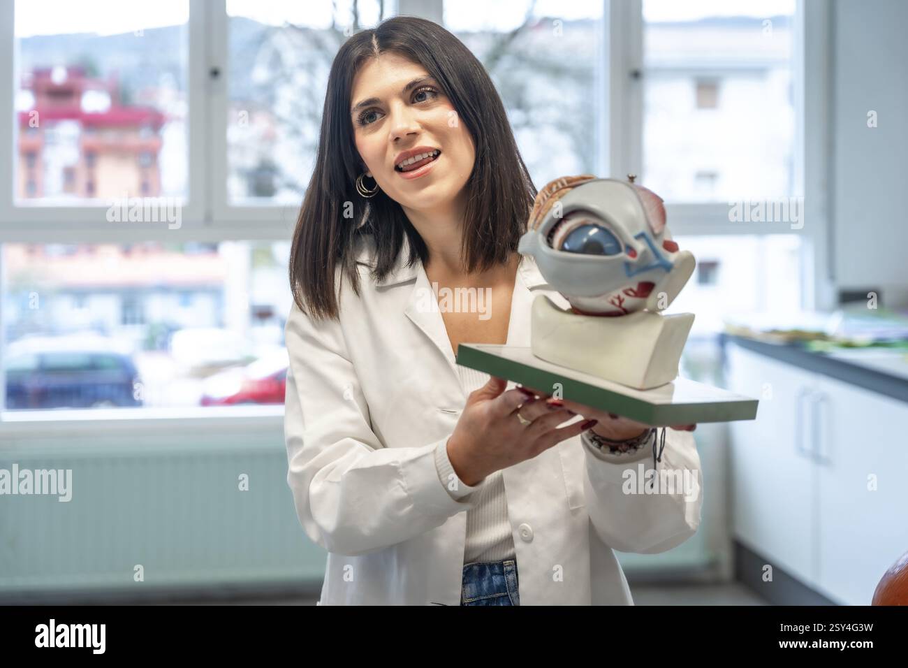 Young woman wearing lab coat holding anatomical model of eye and optic ...