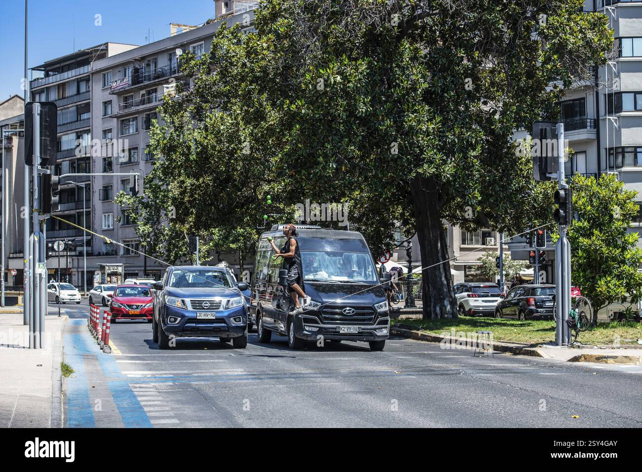 Street artist dances on a rope and juggles between two traffic lights ...