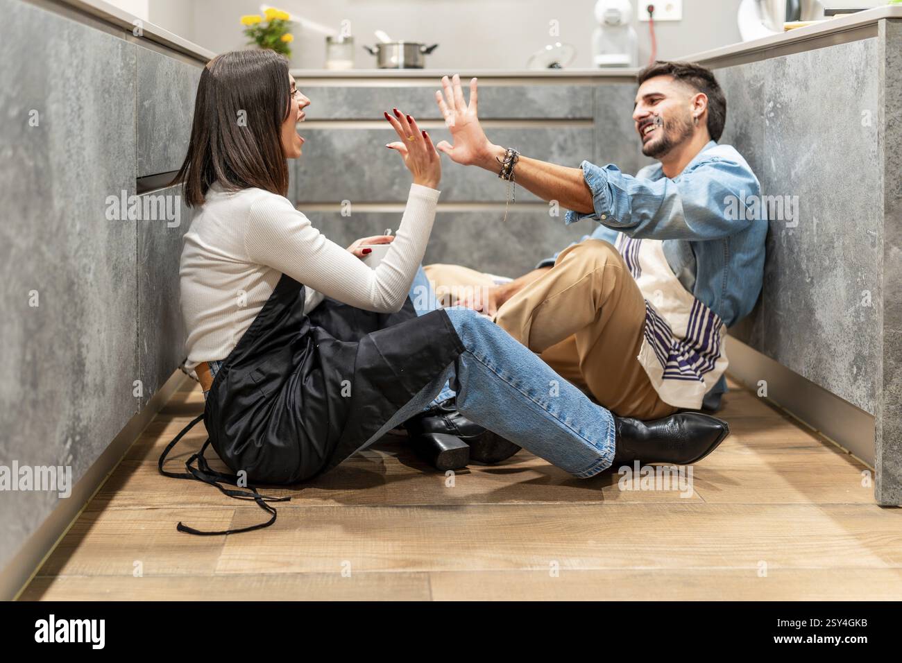 Two young chefs are sitting on the kitchen floor, giving each other a ...