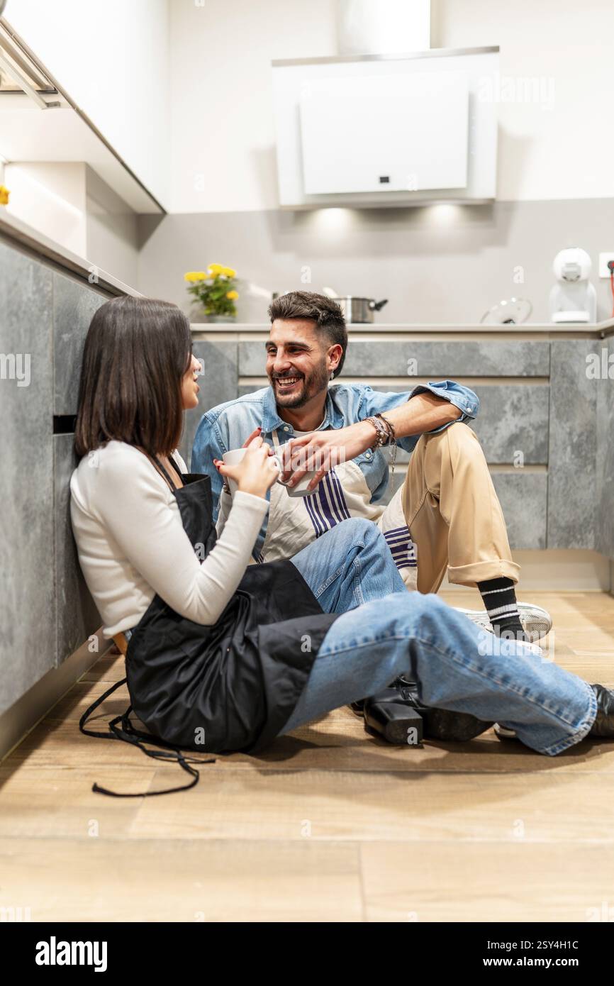 Two chefs are sitting on the floor of a modern kitchen, wearing aprons ...