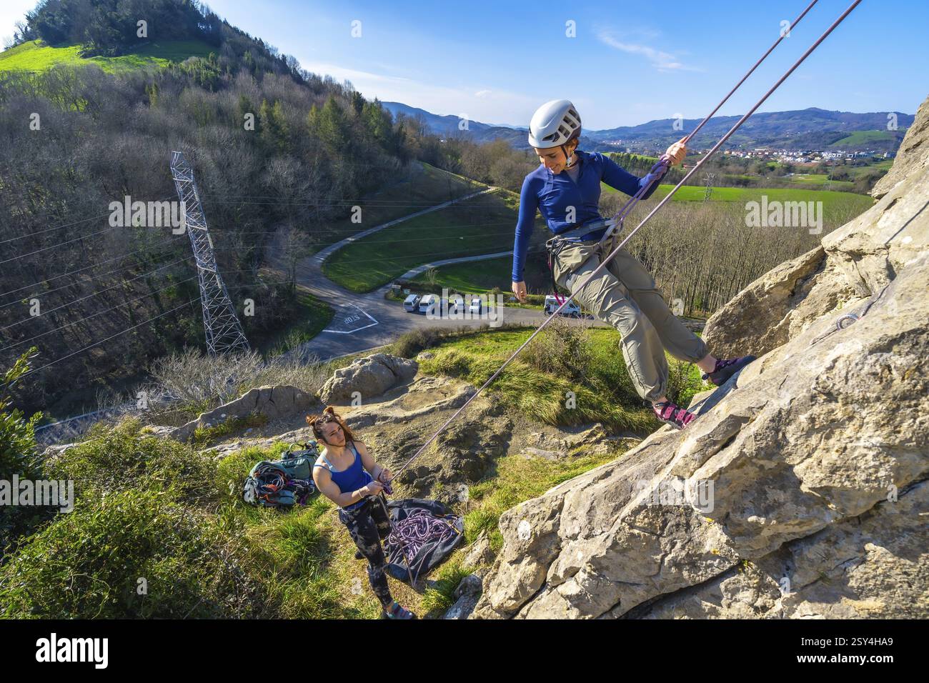Two female rock climbers scaling a cliff face, one ascending while the ...