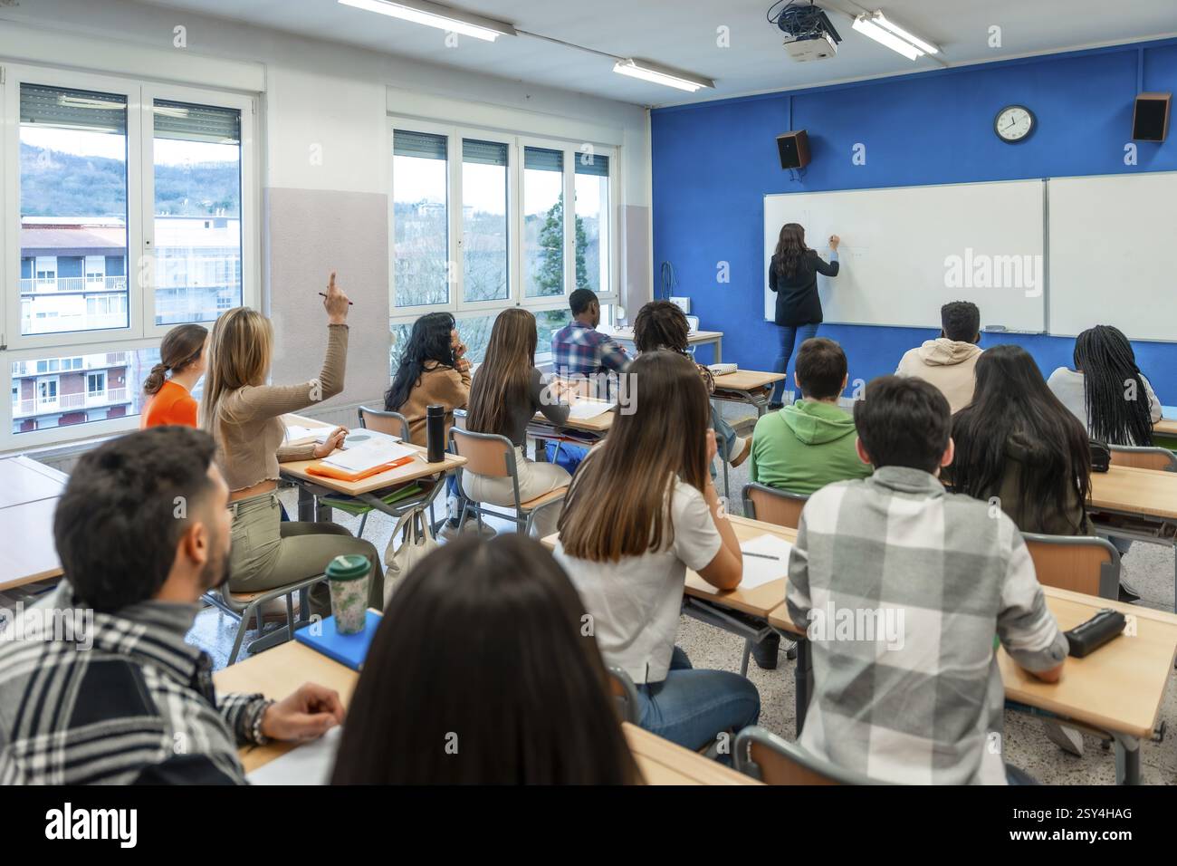 Multi ethnic university students listening to their teacher and raising ...