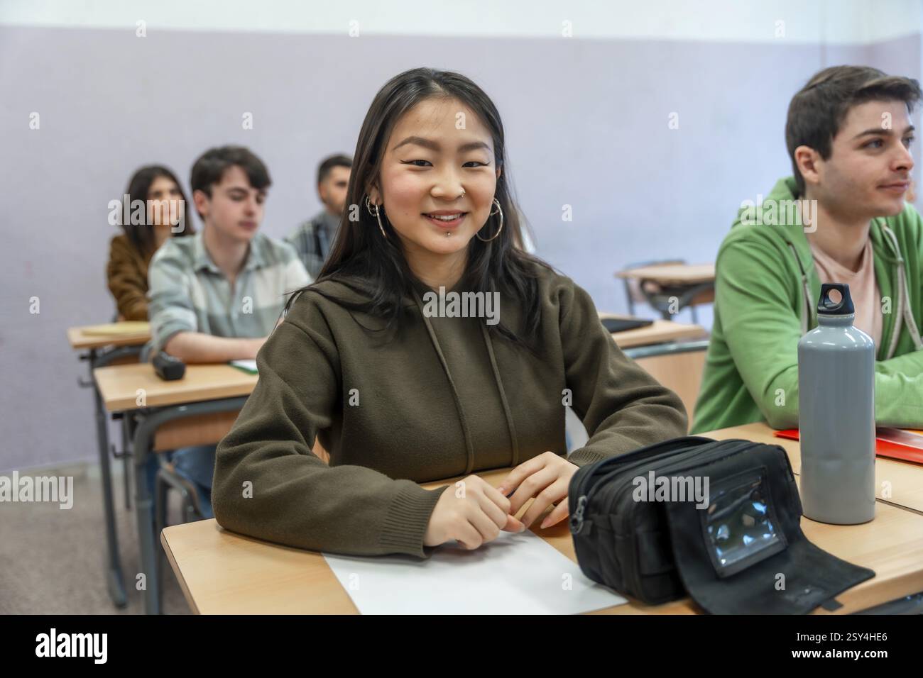 Young asian student smiling while engaging in a lesson with classmates ...