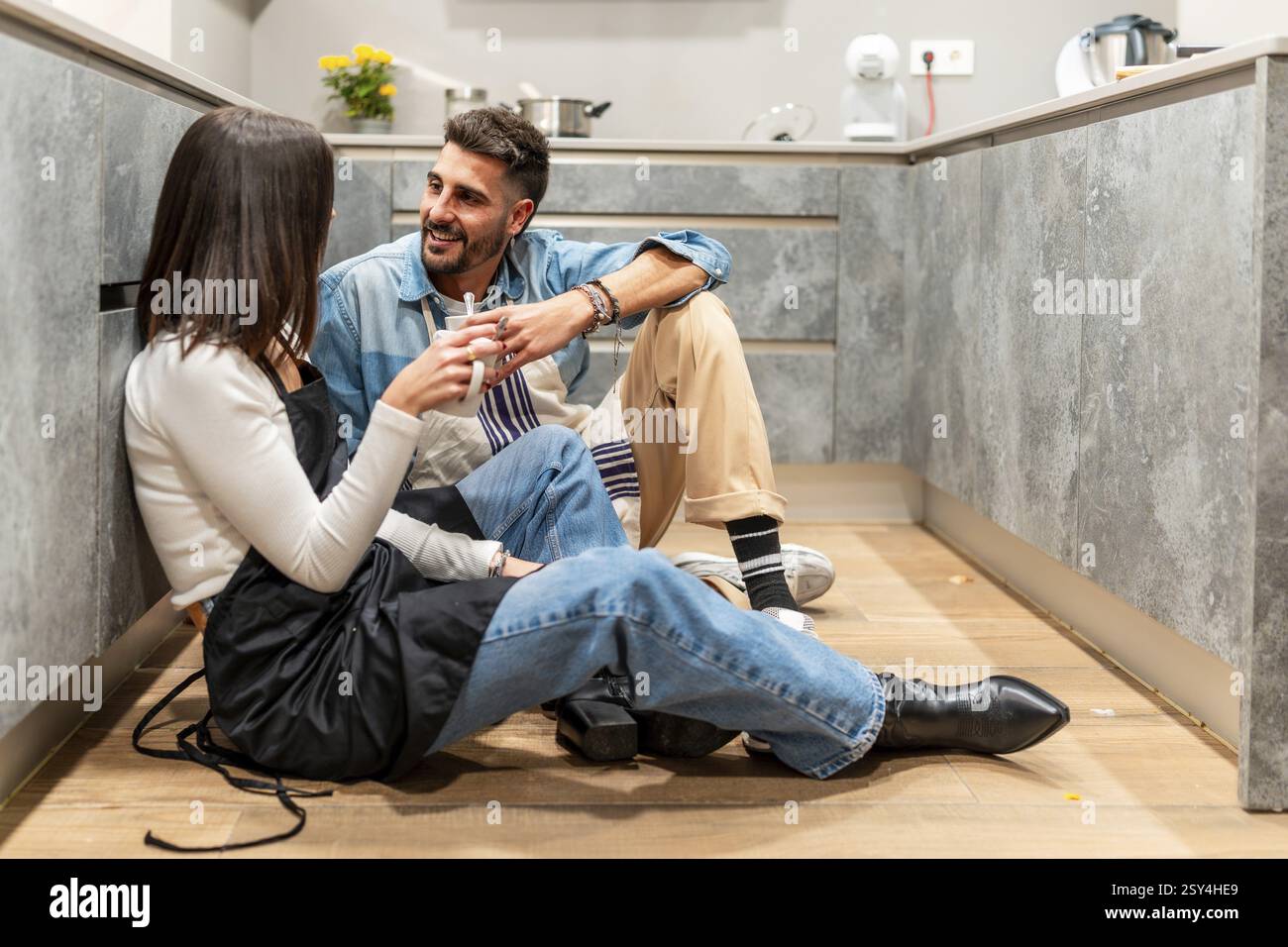 Two chefs are sitting on the floor of a modern kitchen, taking a break ...