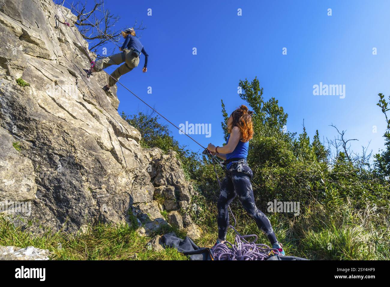 Two female rock climbers ascending a steep cliff face, utilizing ropes and harnesses for safety ...