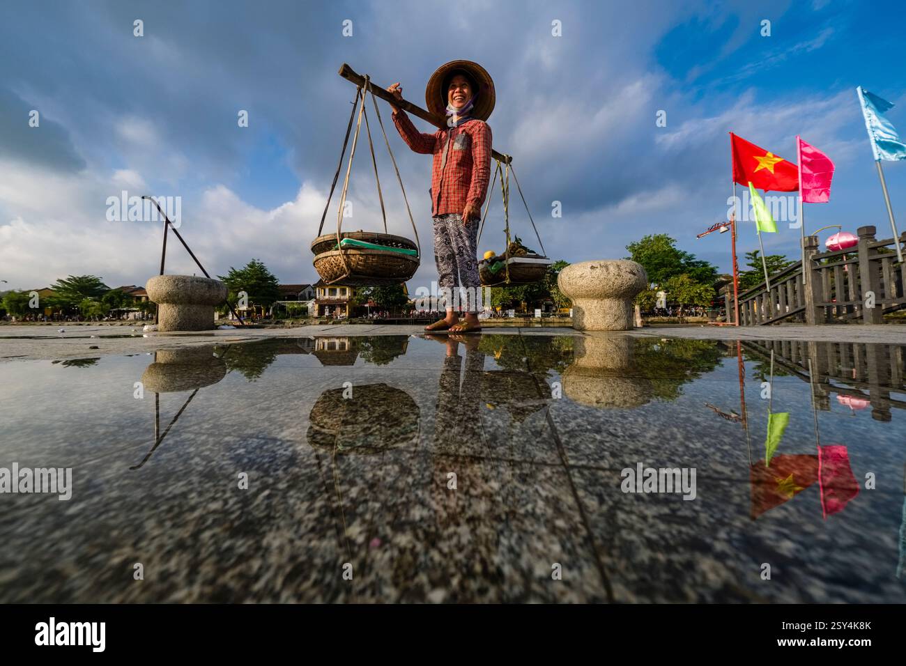 A fruit vendor with a conical hat stands next to a bollard on the Thu ...