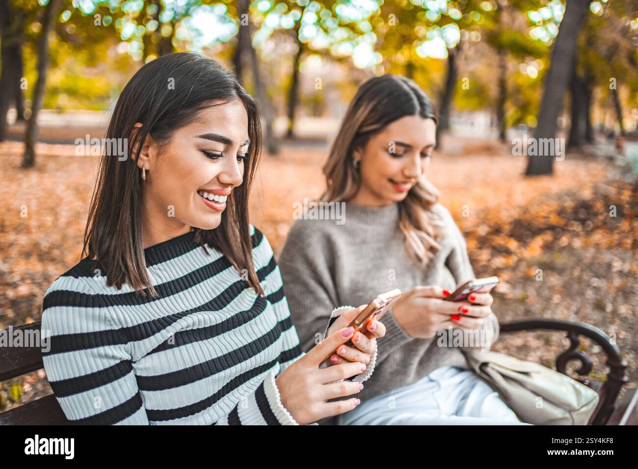 Two Women Sitting on a Bench Looking at Their Phones Stock Photo - Alamy
