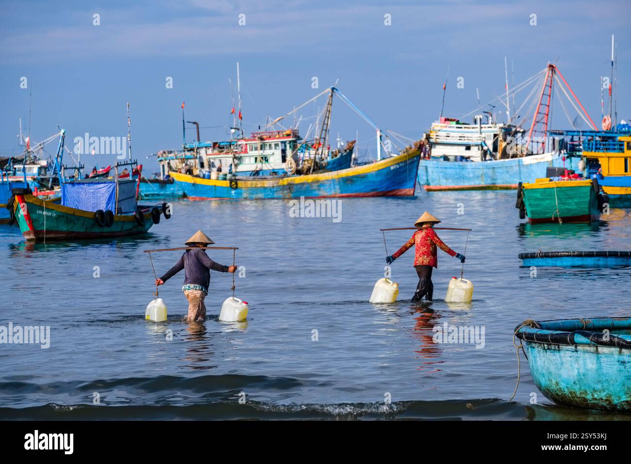 Two women with conical hats carry water in canisters in the water in ...