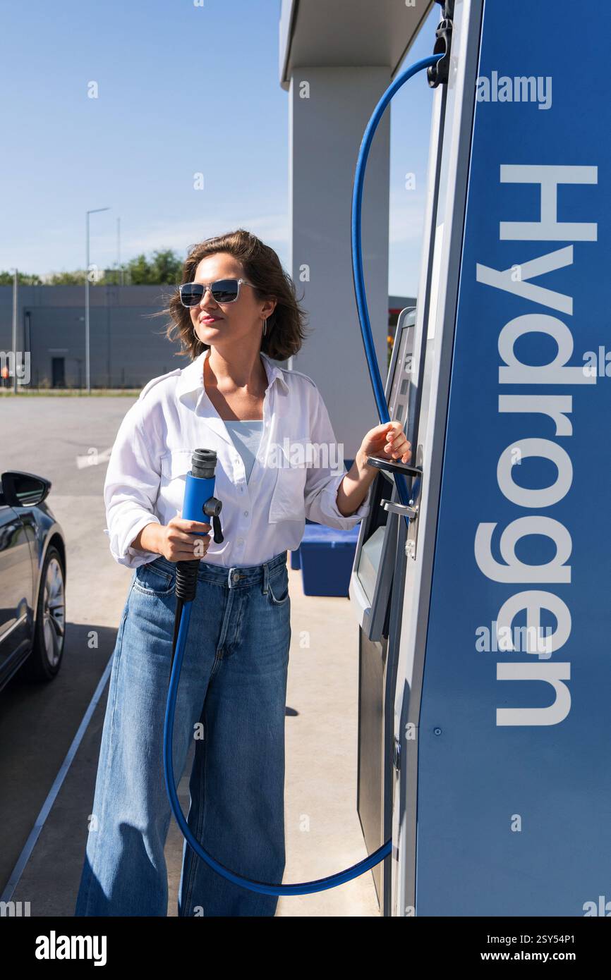 Woman holds a hydrogen fueling nozzle on a hydrogen filling station ...