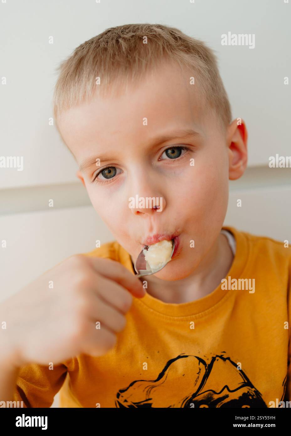 a 4-year-old blond boy eats honey from a spoon with his mouth open ...