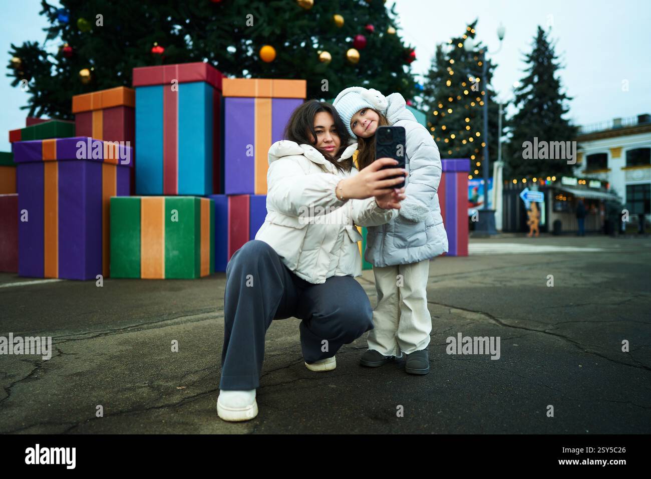 Two girls happily pose for a selfie in front of bright holiday gifts ...