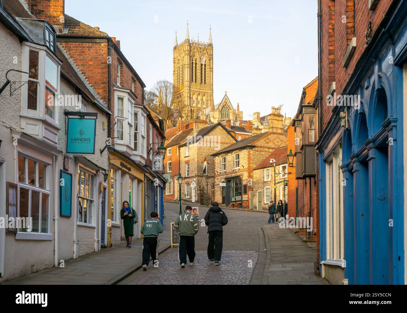 People walking up Steep Hill in evening light, cathedral tower rising ...