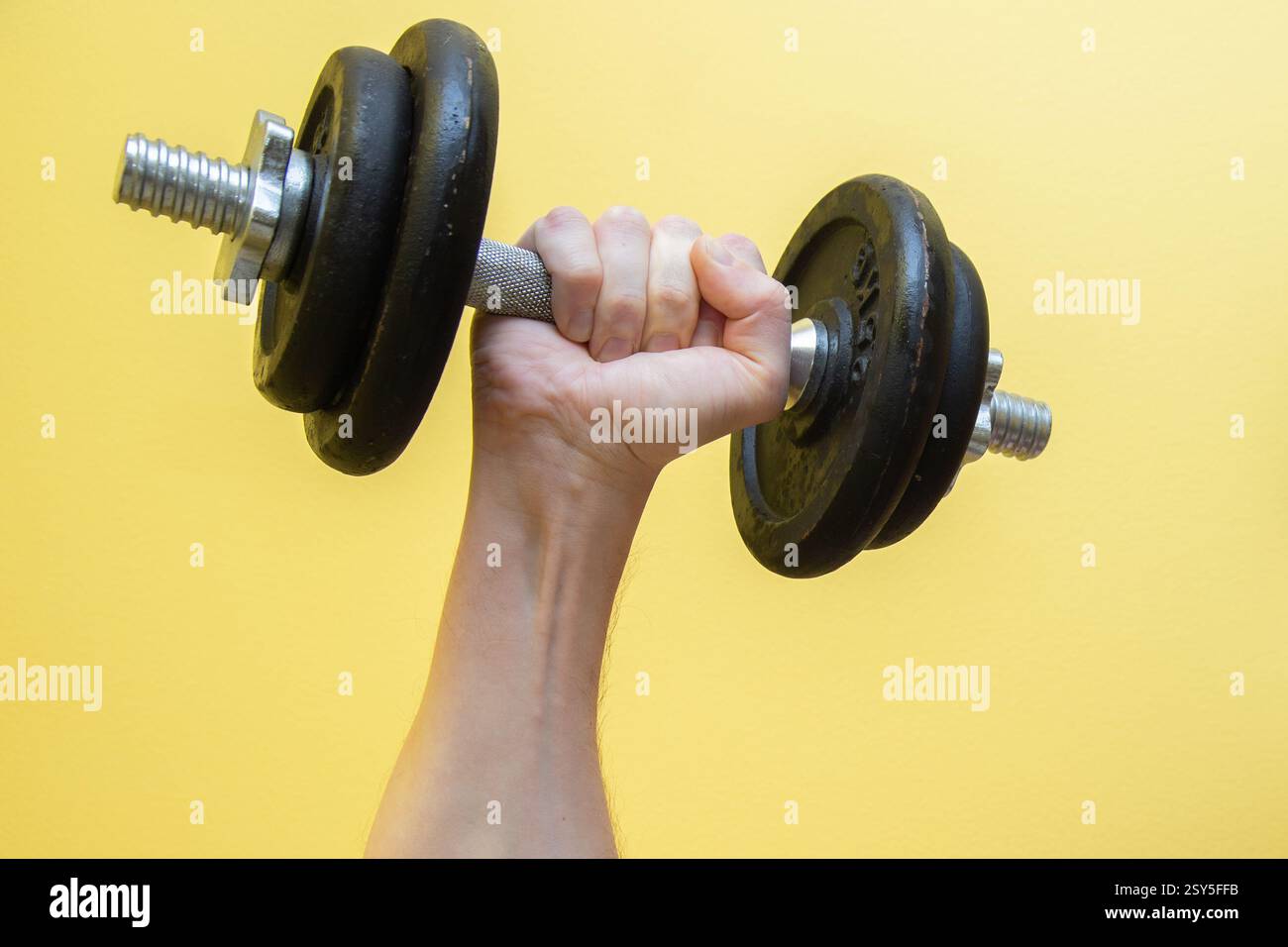 Strong hand holding a dumbell on yellow background. Cropped photo Stock ...
