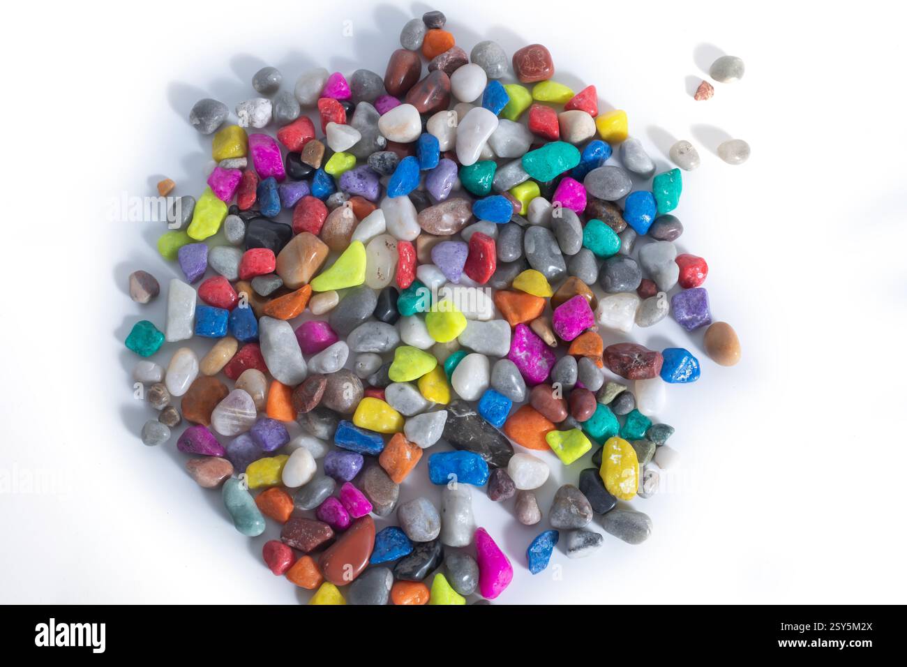 Brightly colored pebbles are stacked on a plain white surface, showing ...