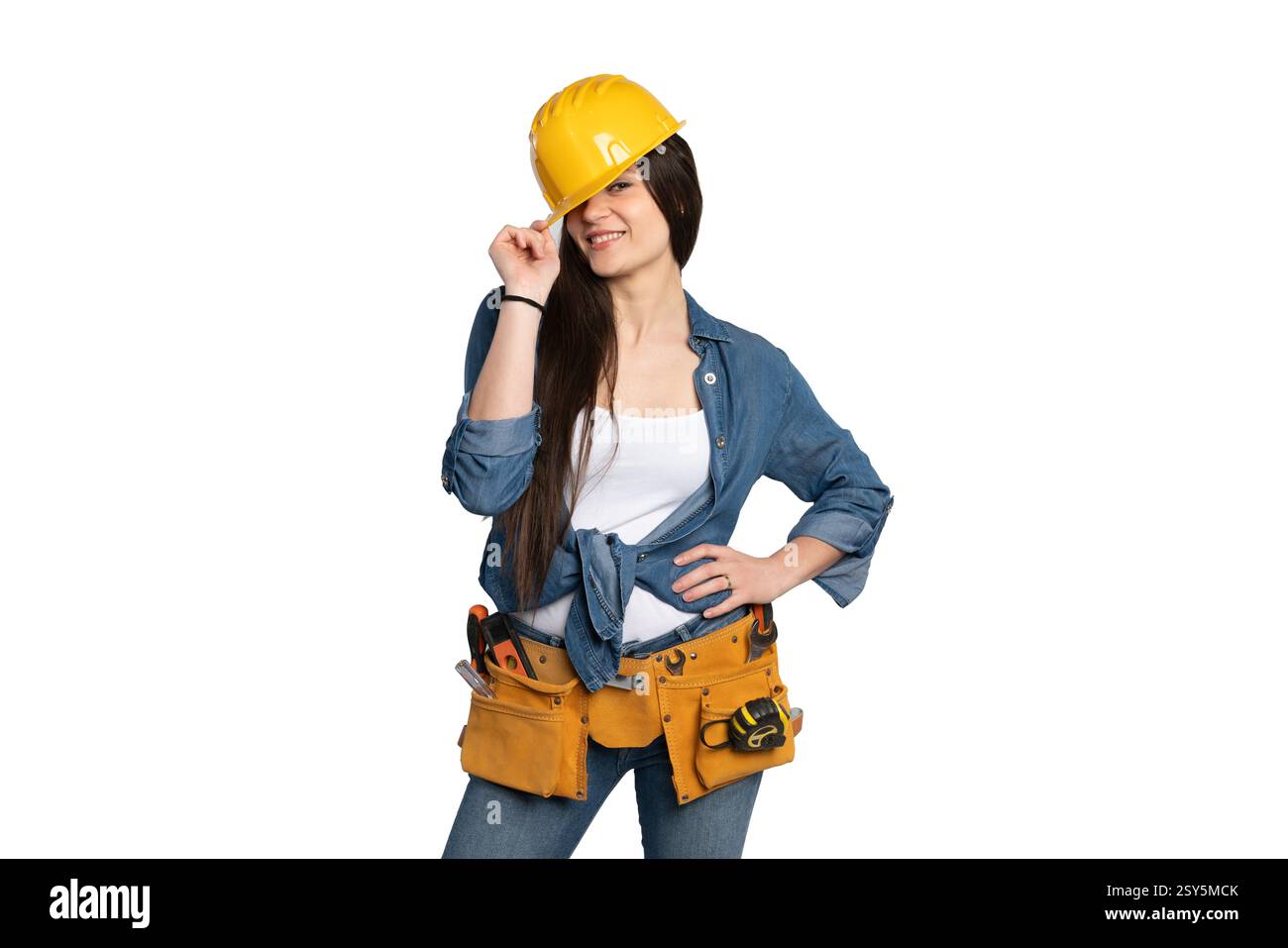 A cheerful female construction worker wearing a yellow safety helmet, denim shirt, and tool belt ...