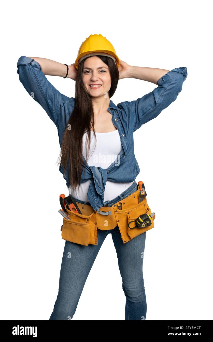 A smiling female construction worker wearing a yellow safety helmet, denim shirt, and tool belt ...