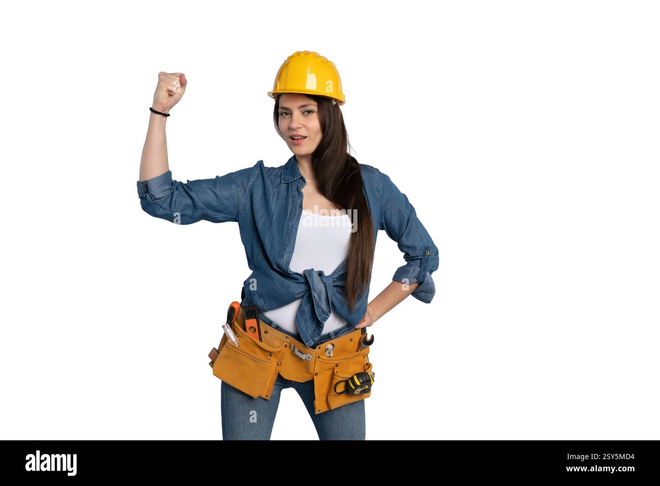 A determined female construction worker wearing a yellow safety helmet, denim shirt, and tool ...