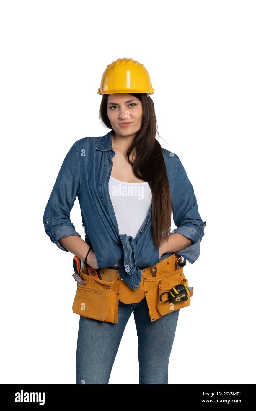 A confident female construction worker wearing a yellow safety helmet, denim shirt, and tool ...