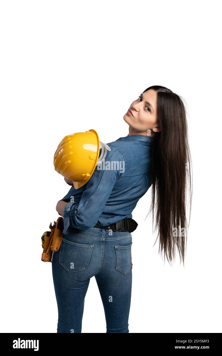 A confident female construction worker wearing a denim shirt and tool belt, posing with a yellow ...