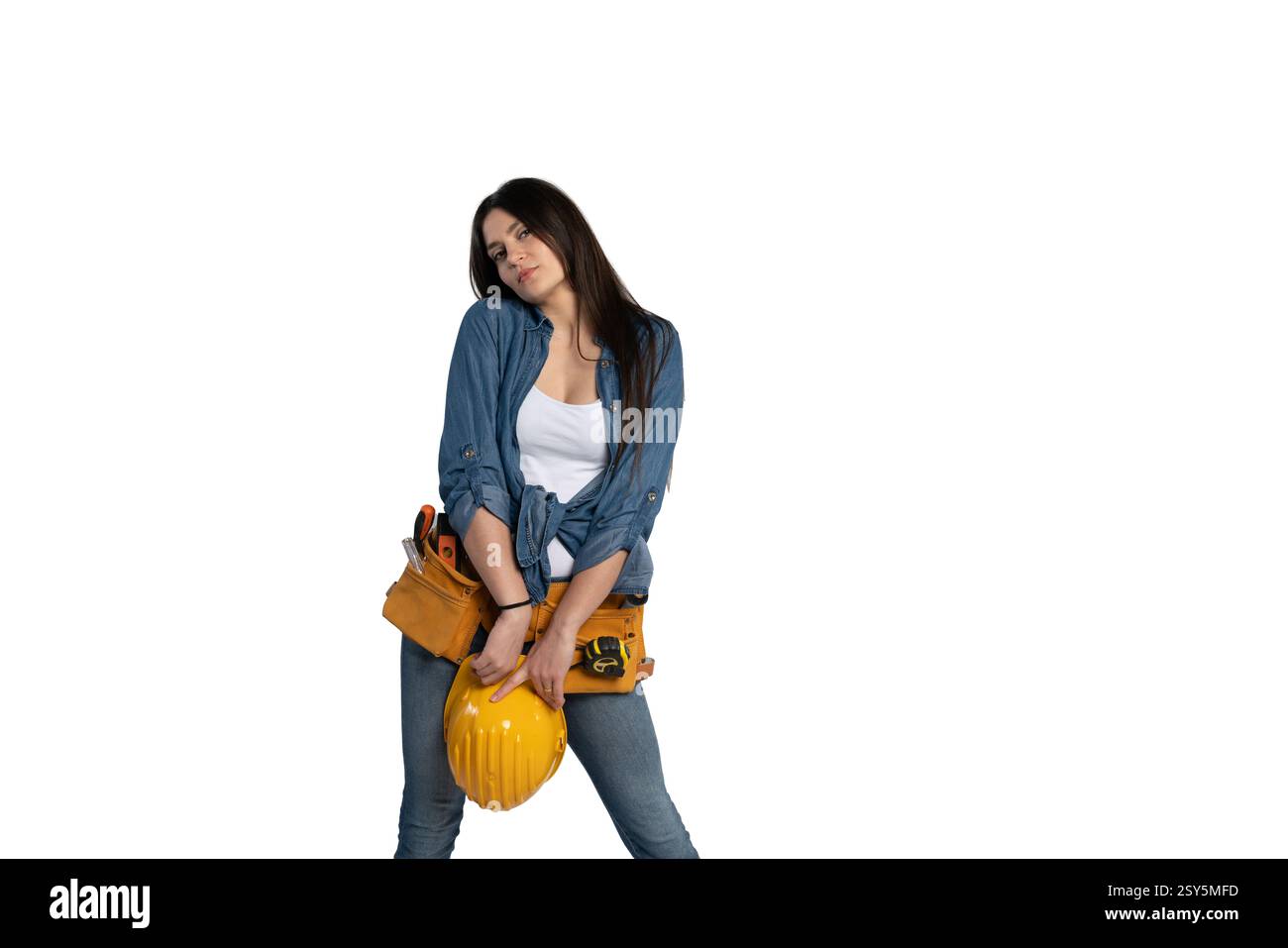A young female construction worker dressed in a denim shirt, white tank top, and tool belt ...
