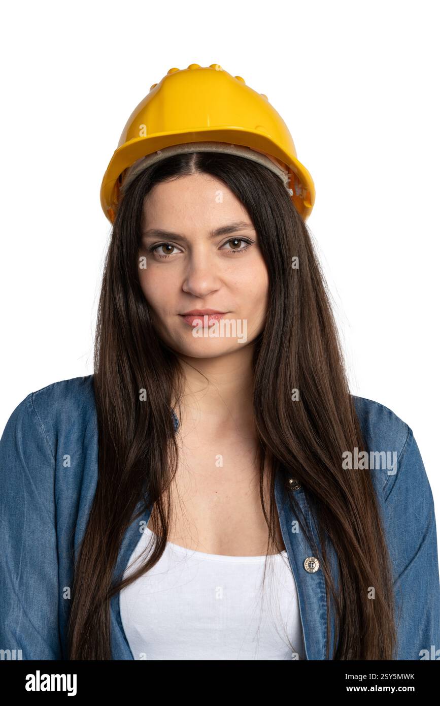 A close-up portrait of a young female construction worker wearing a yellow safety helmet, denim ...