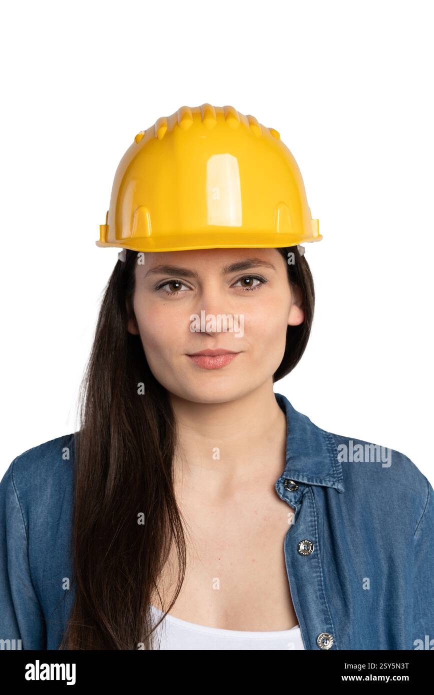 A close-up portrait of a young female construction worker wearing a bright yellow hard hat and a ...