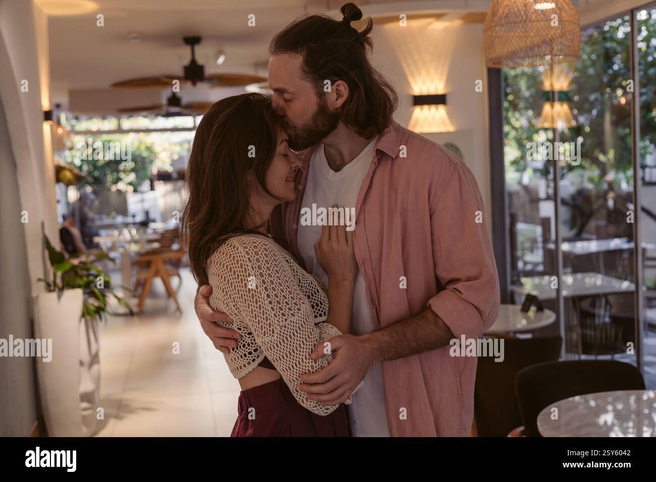 A couple shares an intimate embrace in a cozy cafe. They gaze at each ...