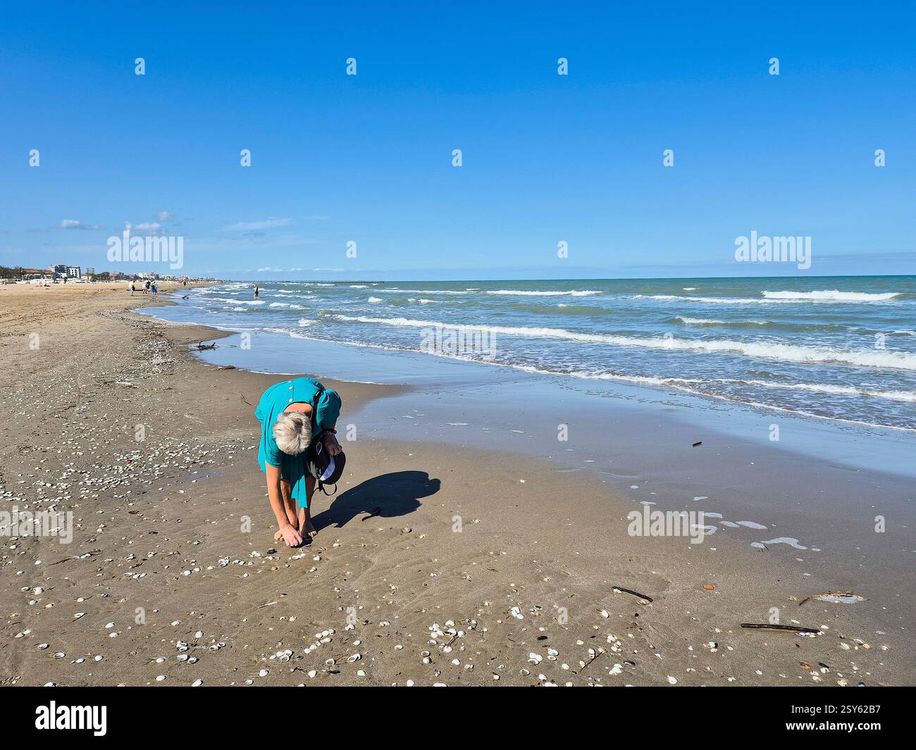 Italy. Miramare di Rimini. old woman collecting shells on the beach ...