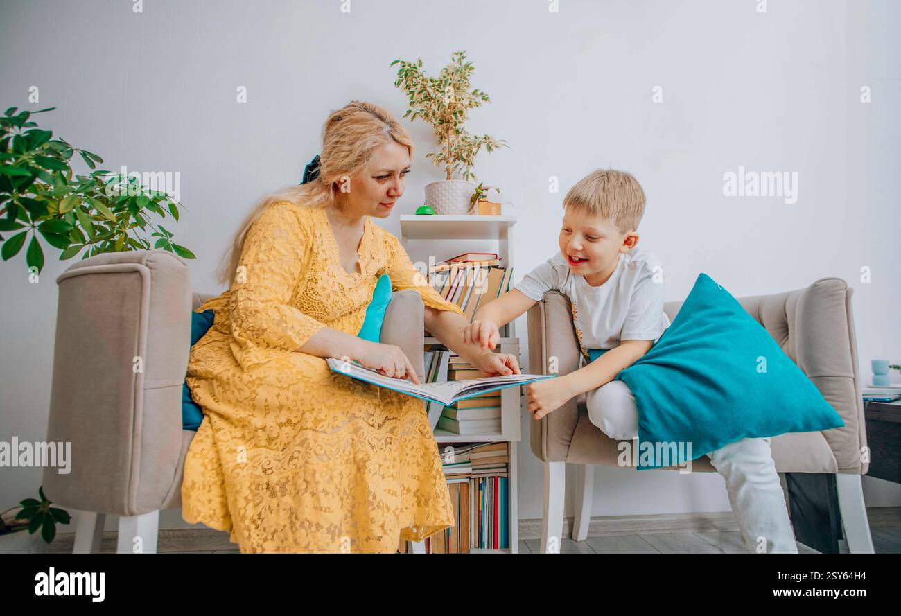 woman in yellow dress reading a book to a smiling boy with blue pillow ...