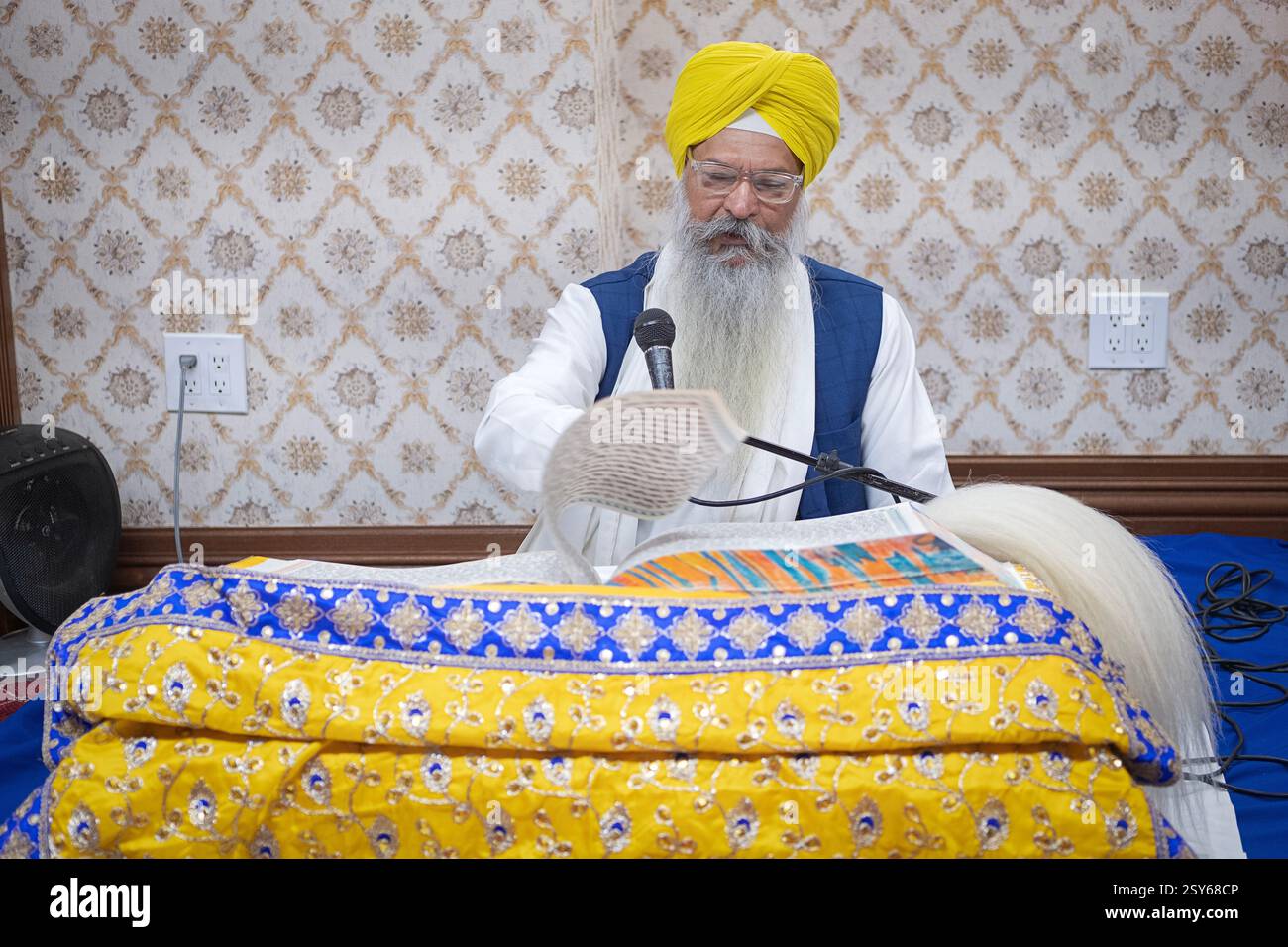 A Sikh priest in a yellow turban reads & turns a page of the Guru ...