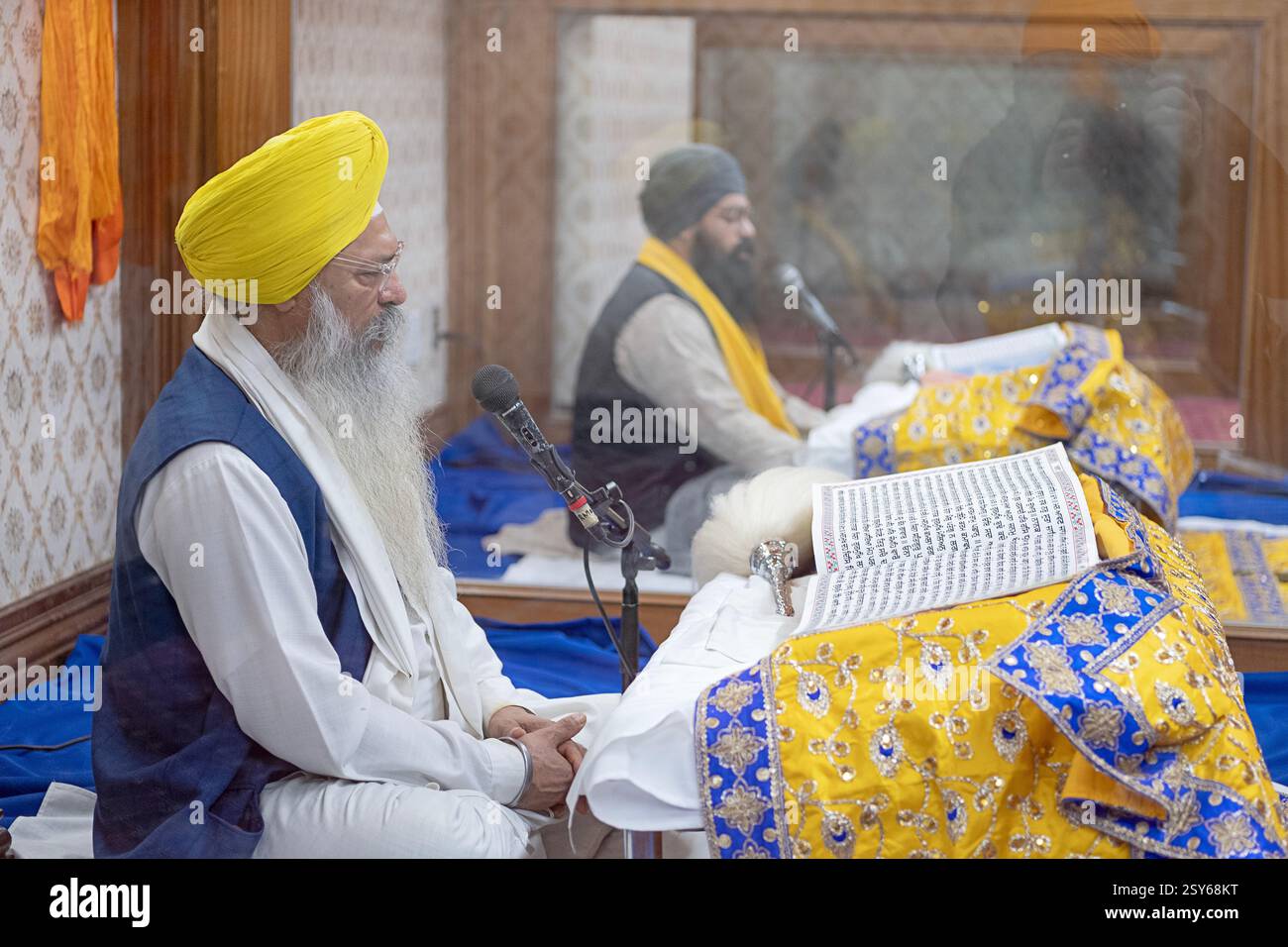 A Sikh priest in a yellow turban reads from the Guru Granth Sahib holy ...