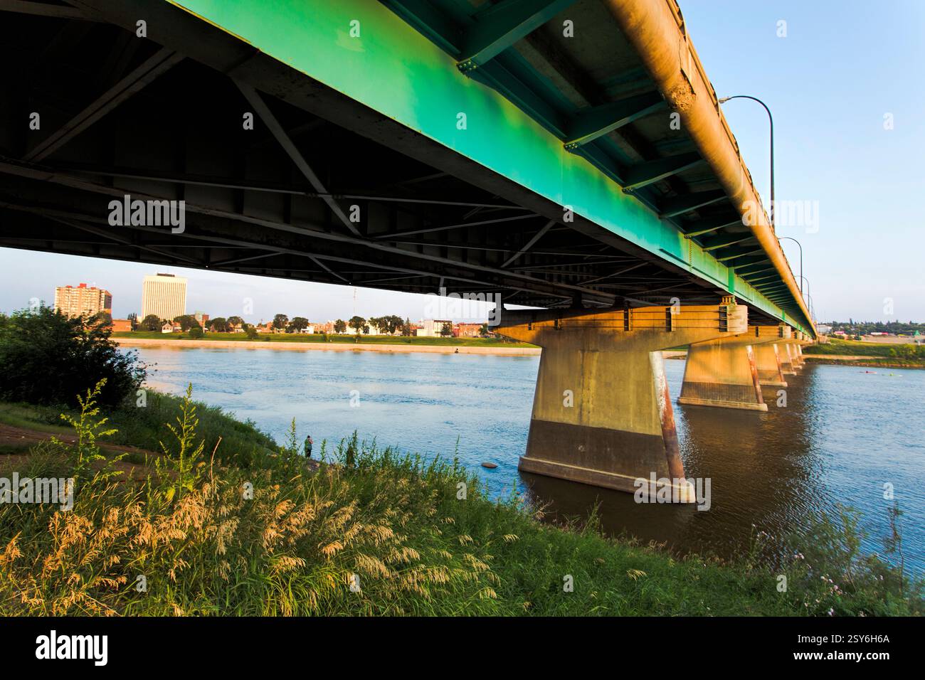 Large green bridge spans across a river, with a city skyline visible in ...
