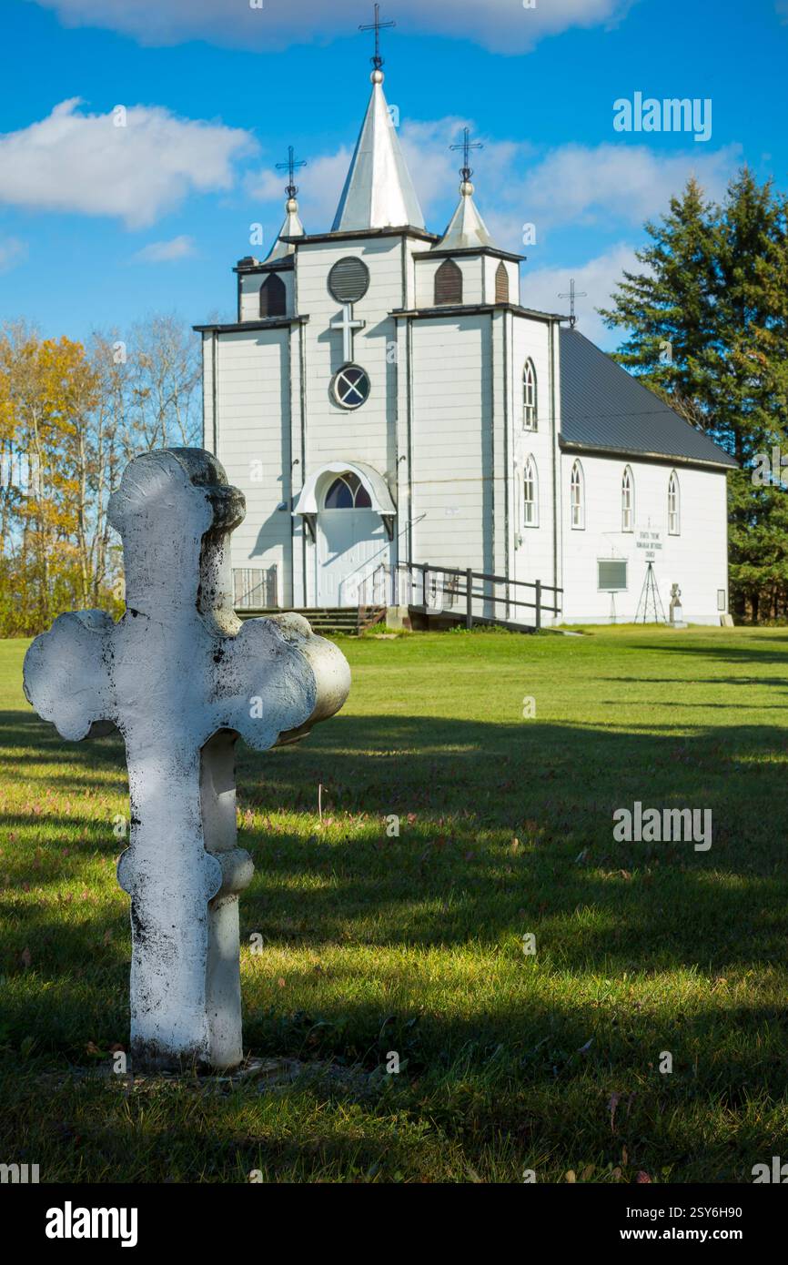 Large white church with a cross in front of it. The cross is white and ...