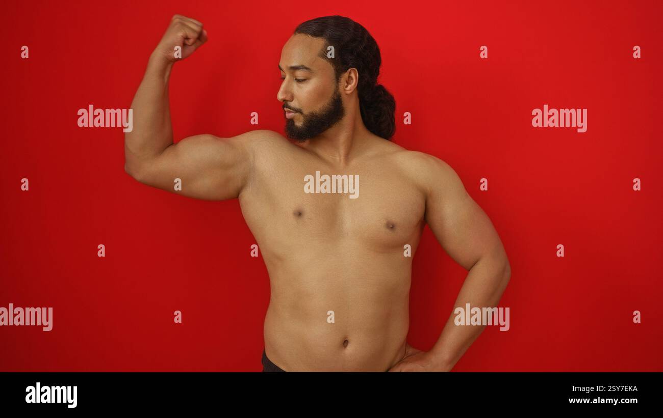 Muscular man posing confidently with flexed bicep against stark red ...