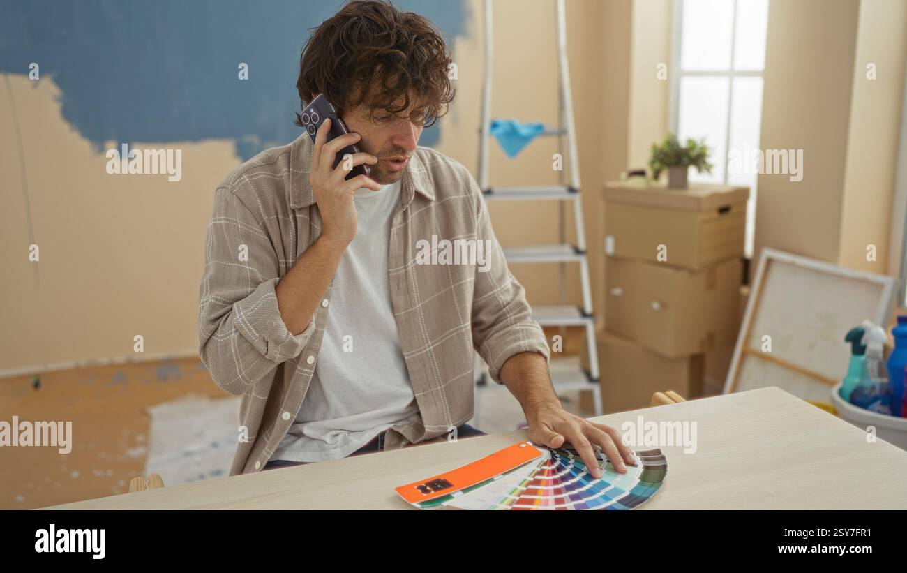 Young man talking on phone while choosing paint colors in a new home ...