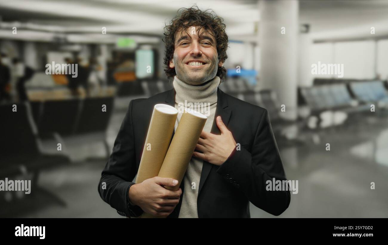 Young man holding document tubes indoors at an airport terminal smiling ...