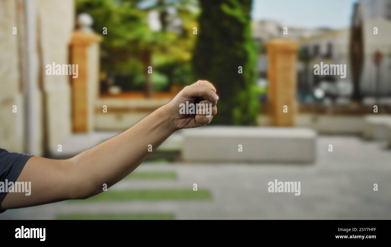 Hand of a man forming a fist against an outdoor city street backdrop ...
