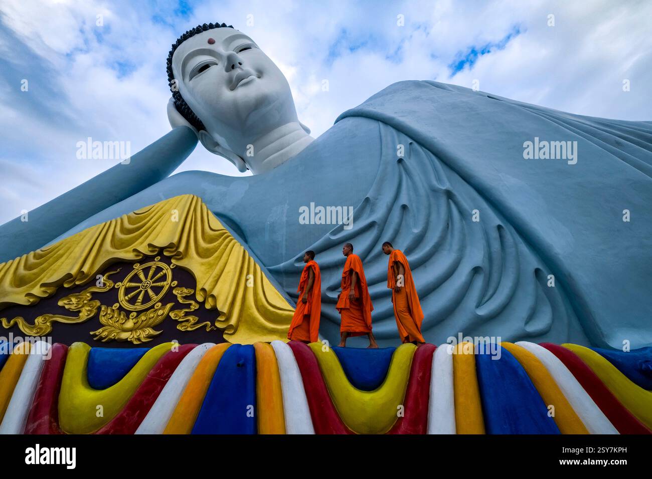 Three buddhist monks walk in front of the 63 metre long statue of a ...