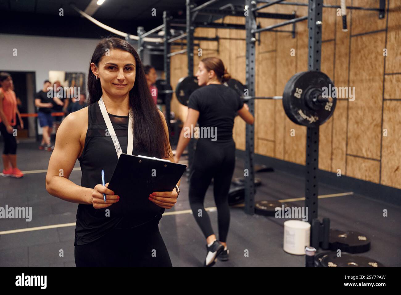 Professional gym trainer is standing indoors with notepad in hands ...