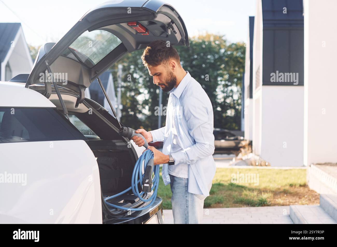 Taking charging wire from the truck. Young stylish man is with electric ...