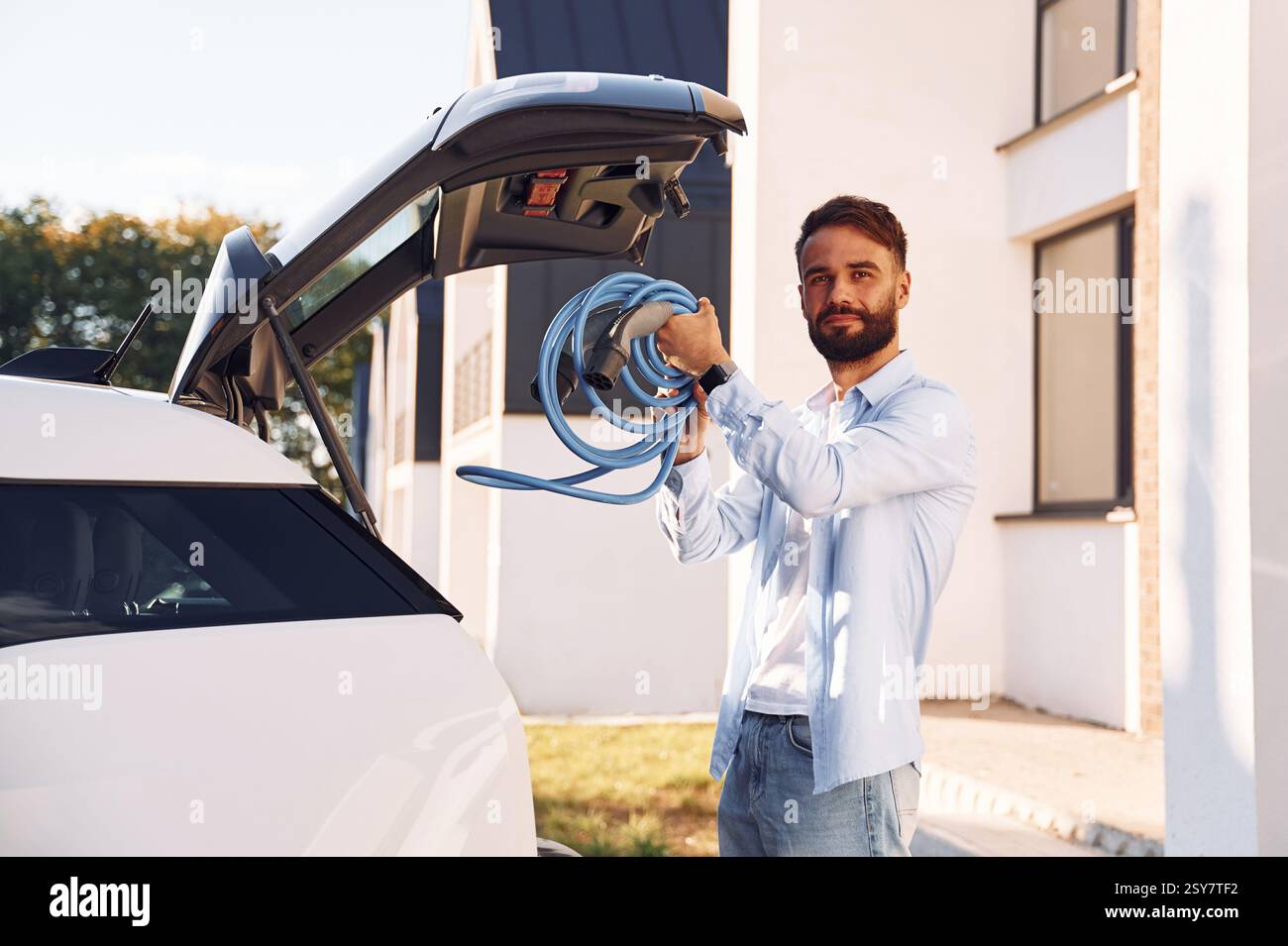 Taking charging wire from the truck. Young stylish man is with electric ...