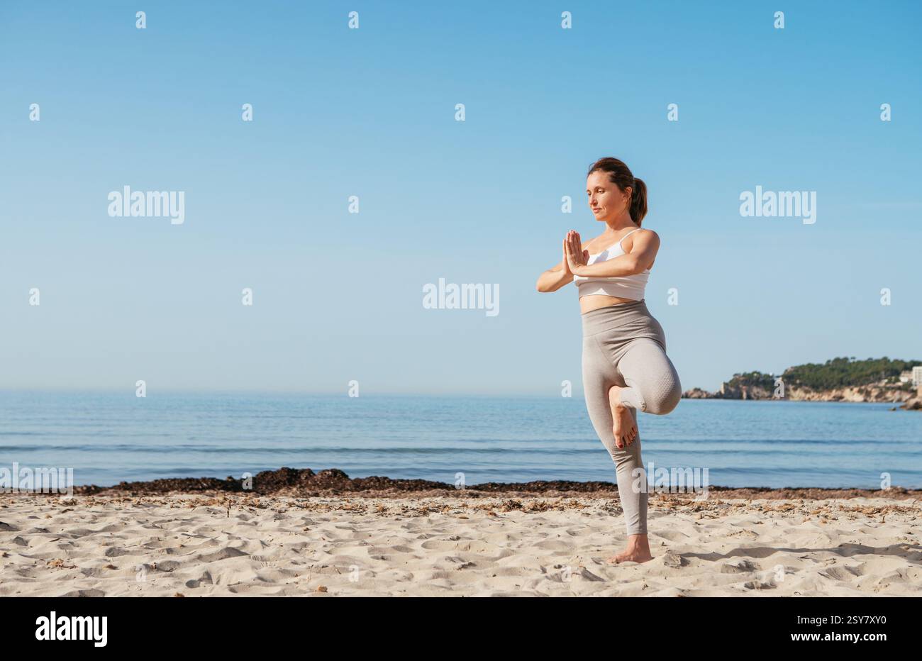 Calm woman standing on one leg doing deep breathing and stratching ...