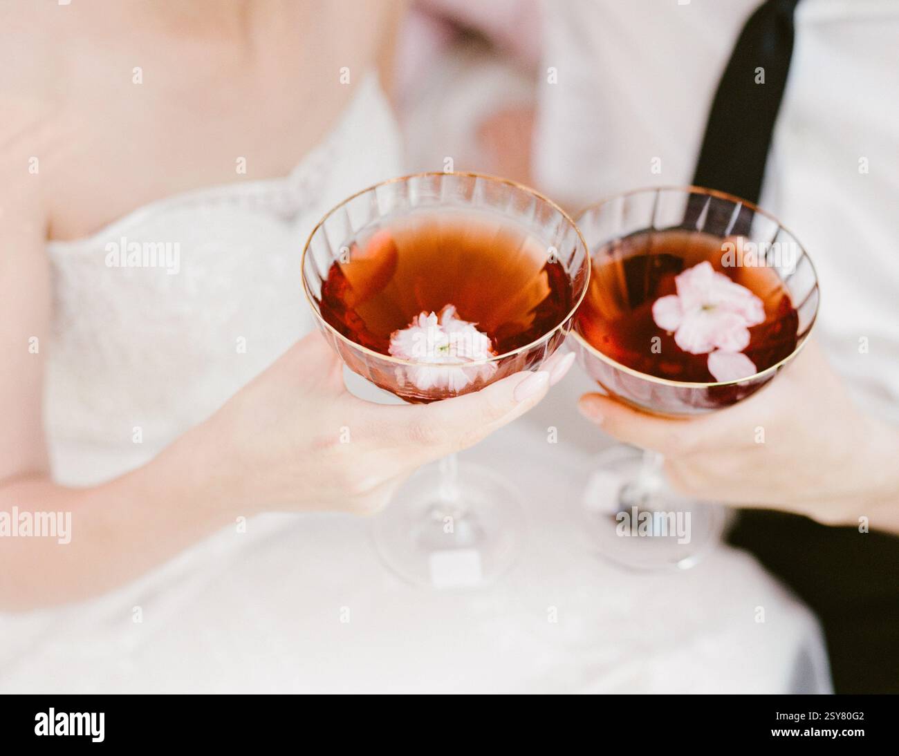 Two elegantly dressed guests toast with floral cocktails during a ...