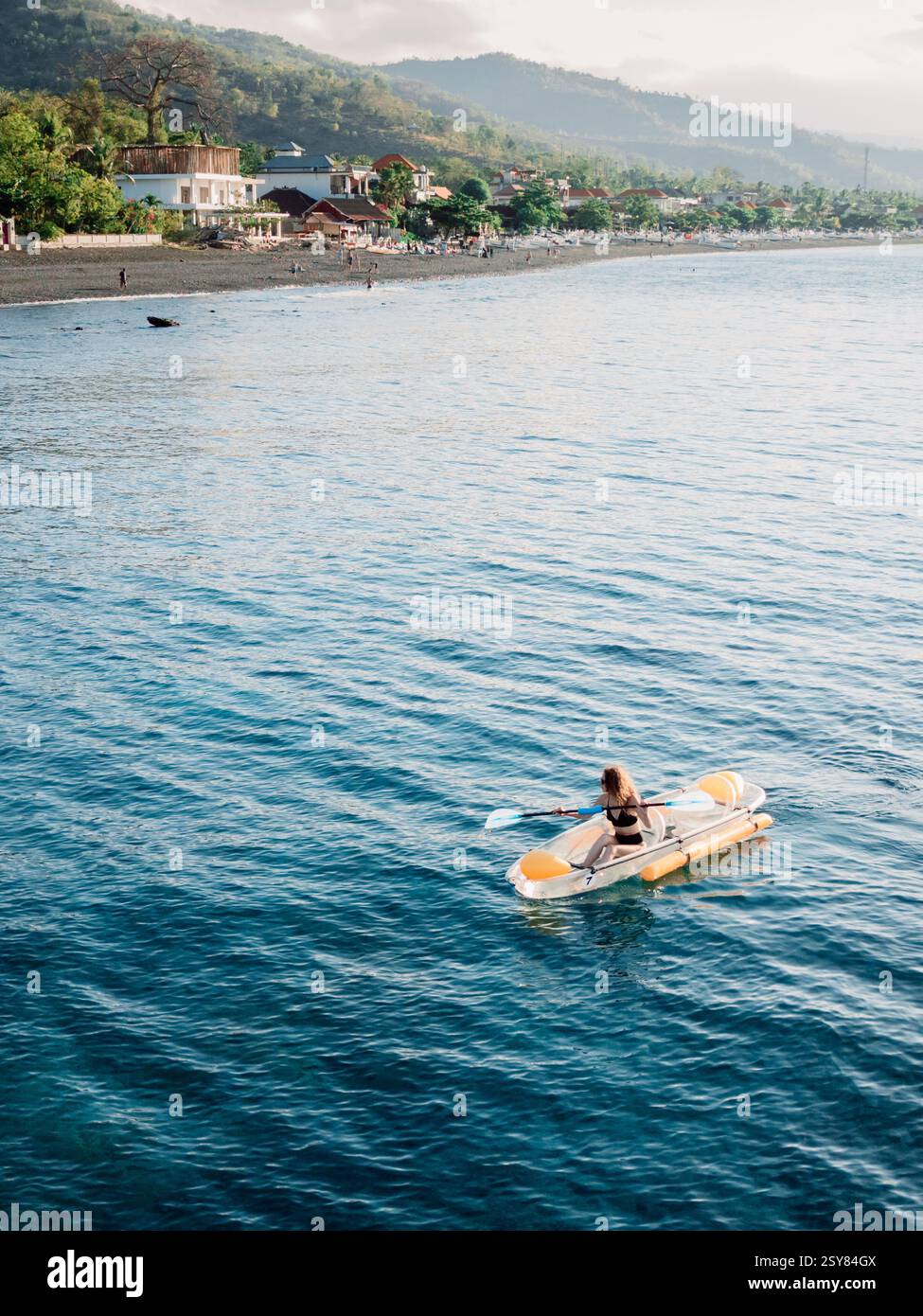 Woman on transparent kayak swims in sea and view of coastal landscape ...