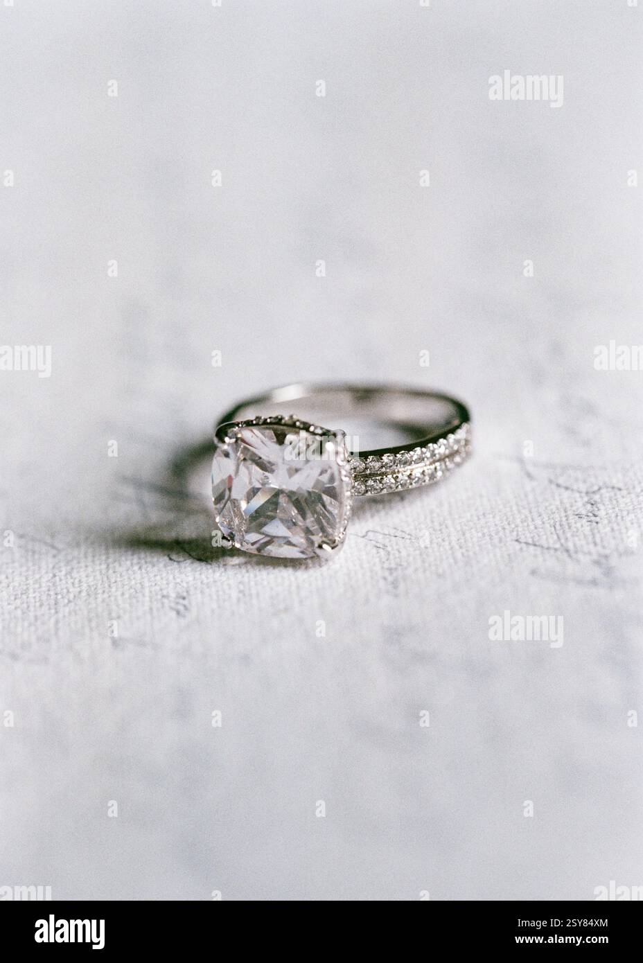 A stunning cushion-cut diamond ring sparkles gently on a textured ...