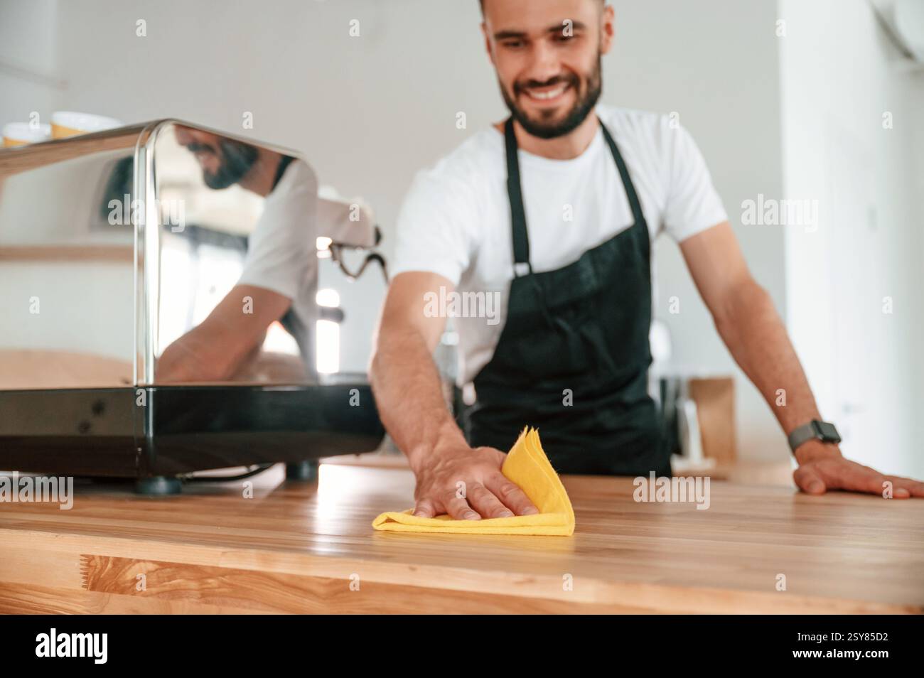 Cleaning table. Cafe worker in white shirt and black apron is indoors ...